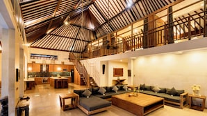 Uma sala de estar ampla com um sofá grande em formato de L, uma mesa de centro de madeira e uma escada que leva a um andar superior.