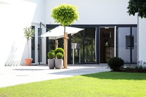 Um edifício moderno com entrada coberta, grandes vasos de plantas e um gramado bem cuidado.