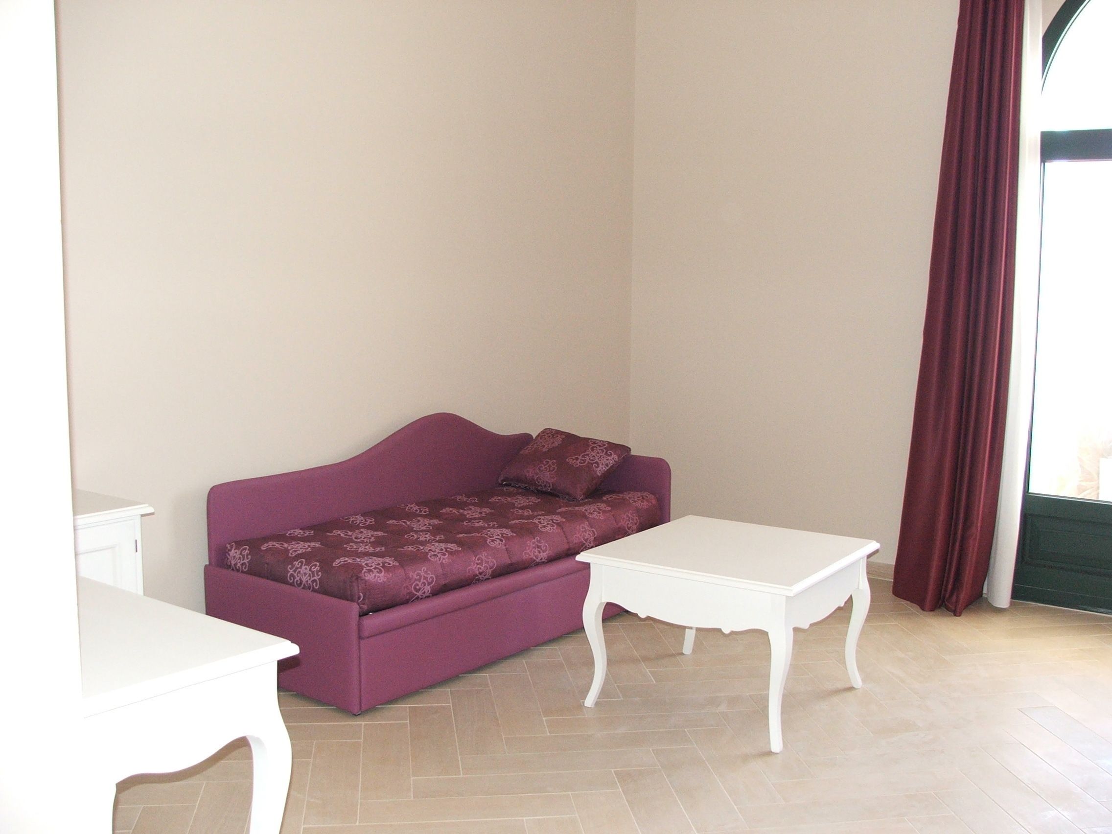 Quarto com um sofá roxo, uma mesa branca e uma janela com cortinas vermelhas.