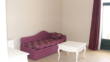 Quarto com um sofá roxo, uma mesa branca e uma janela com cortinas vermelhas.