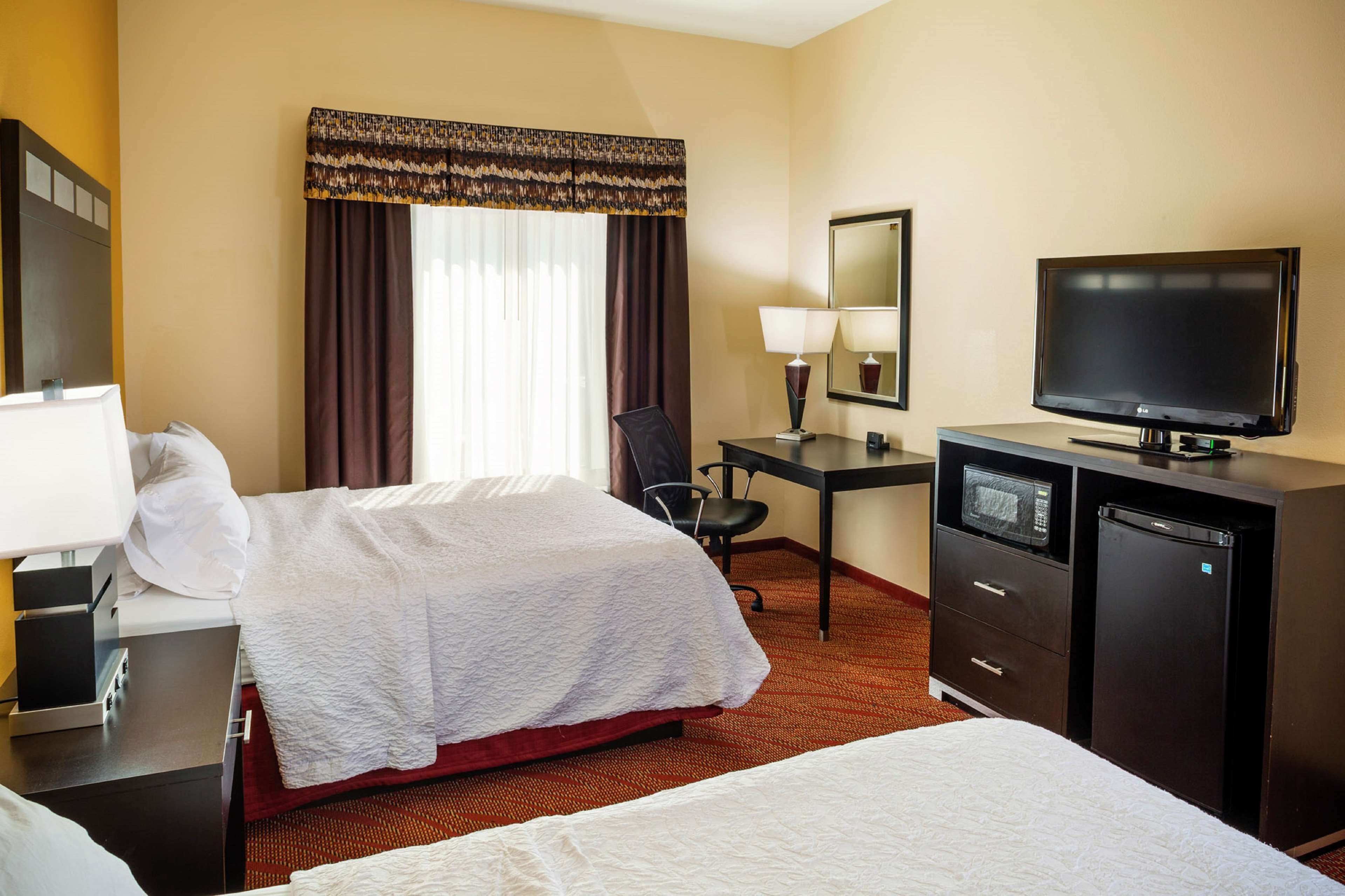 Quarto de hotel com cama, escrivaninha, televisão e micro-ondas.