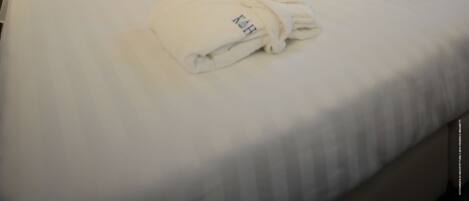 Quarto de hotel com uma cama grande, duas almofadas, mesa de cabeceira com abajur e janela com cortinas.