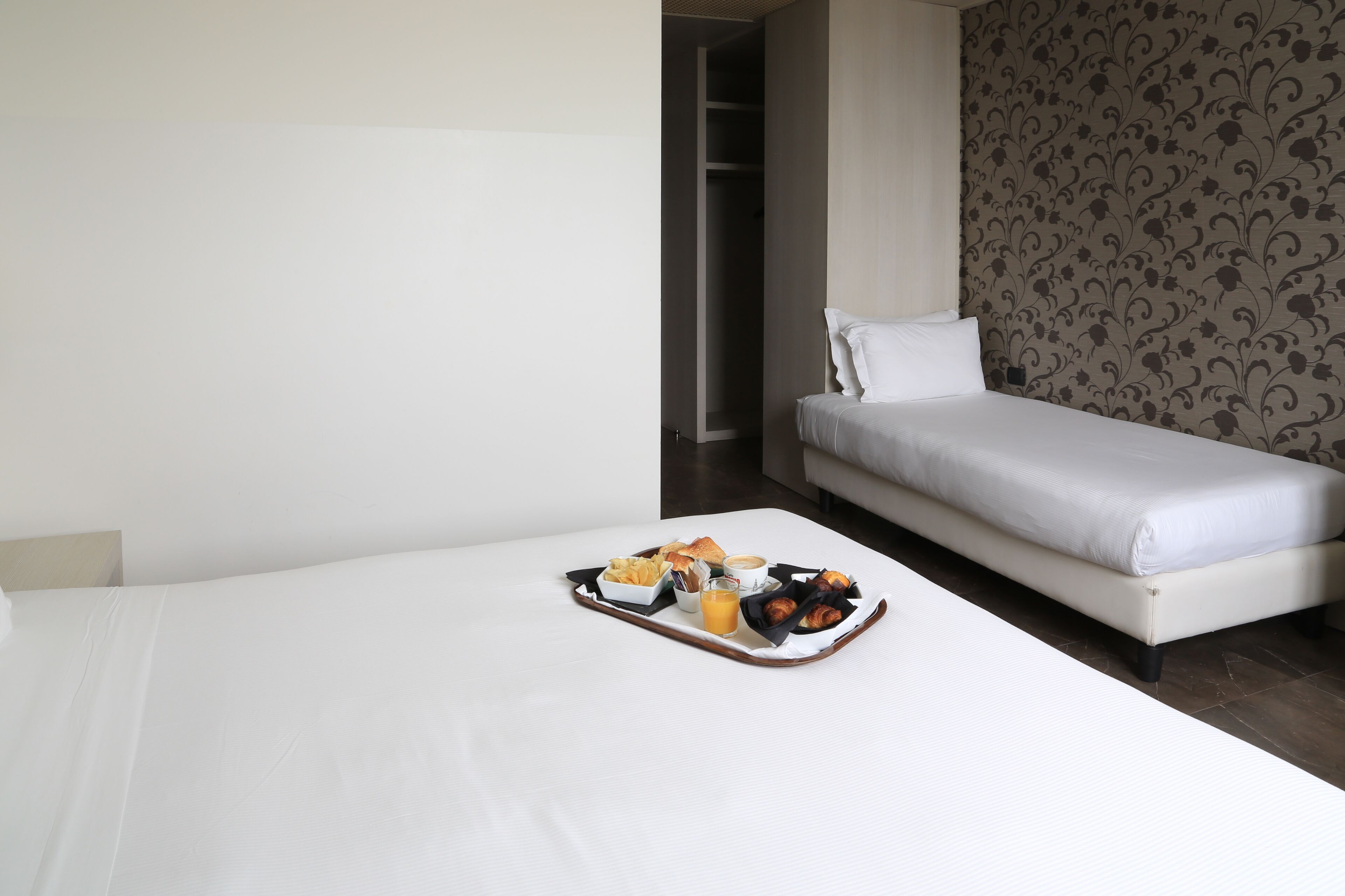 Quarto de hotel com uma cama, um pequeno sofá e uma bandeja com itens de café da manhã.