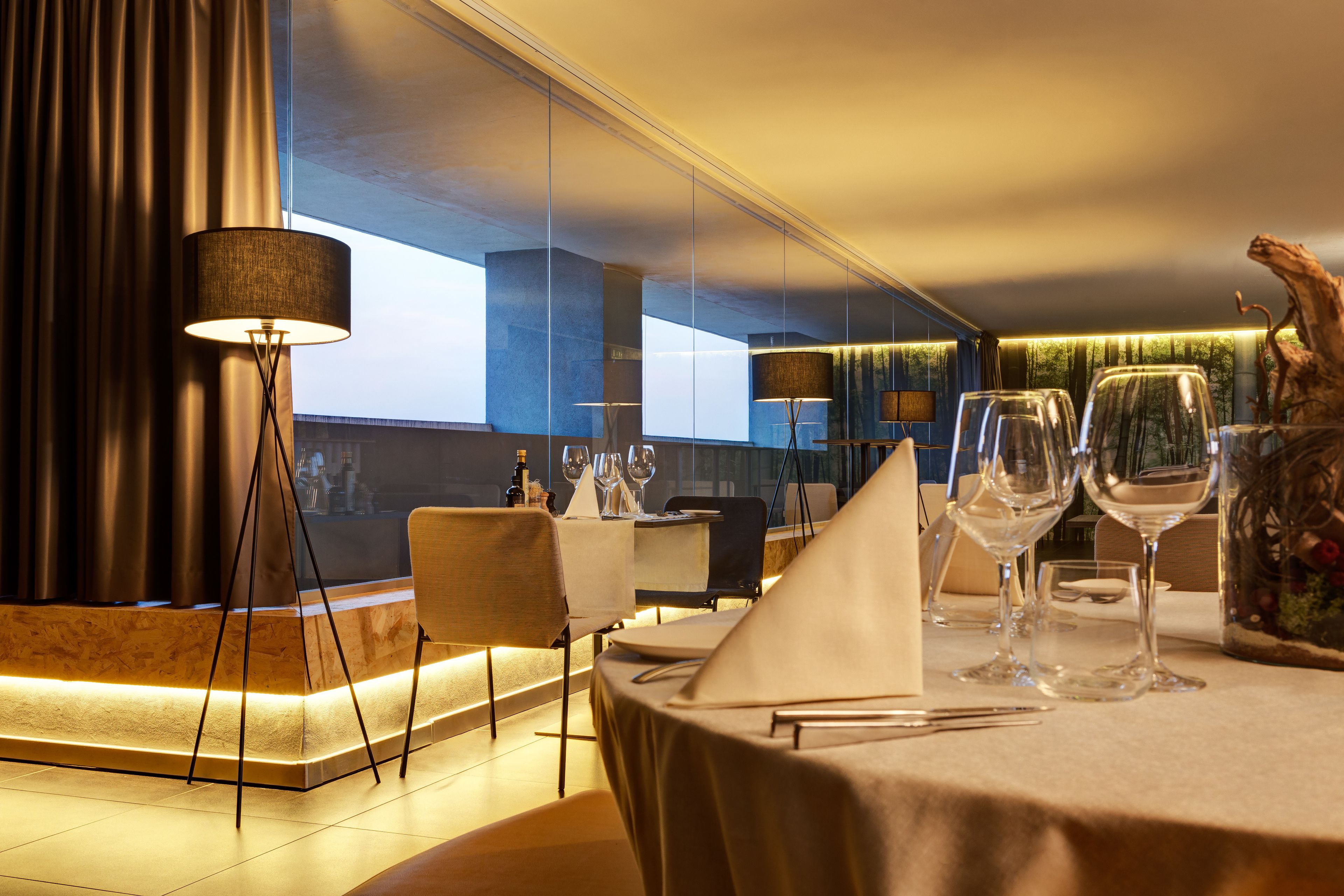 Uma área de jantar moderna com uma mesa posta para dois, uma luminária e taças de vinho.