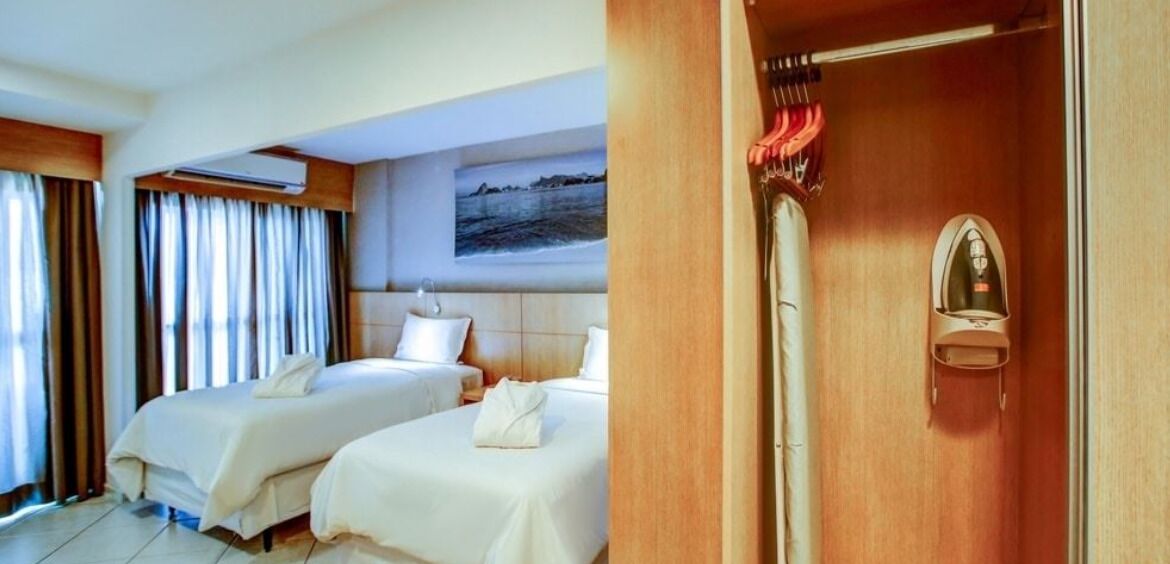 Quarto de hotel com duas camas, um guarda-roupa de madeira e um quadro na parede.