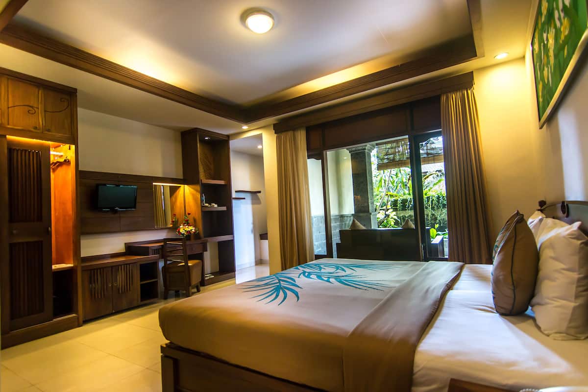 Quarto de hotel com uma cama grande, uma escrivaninha com cadeira, televisão e vista para o verde lá fora.