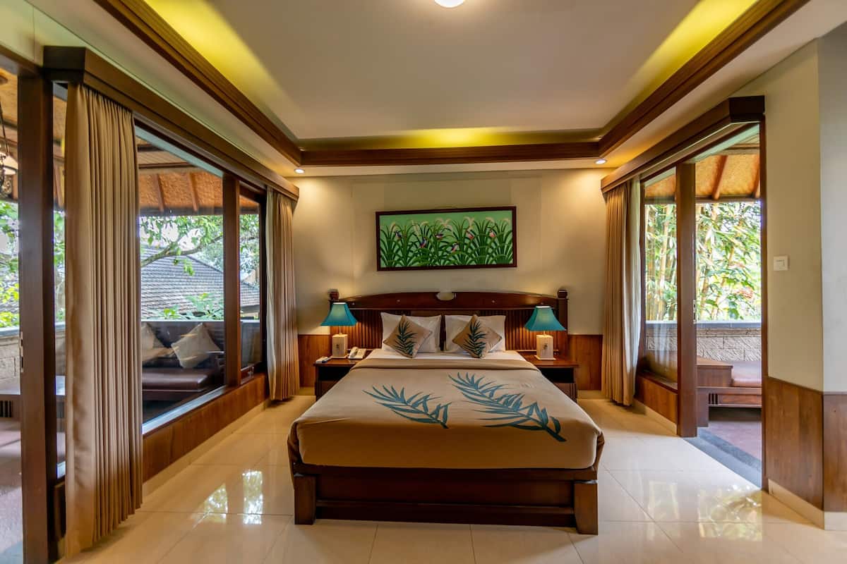 Quarto espaçoso com uma cama grande, cabeceira de madeira e vista para o verde pelas janelas.