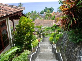 Escadaria que leva a um edifício com telhado de azulejos, cercado por vegetação exuberante e vista para o oceano.