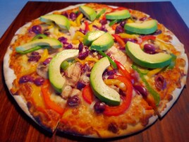 Pizza com diversos ingredientes, incluindo frango, abacate e pimentões.