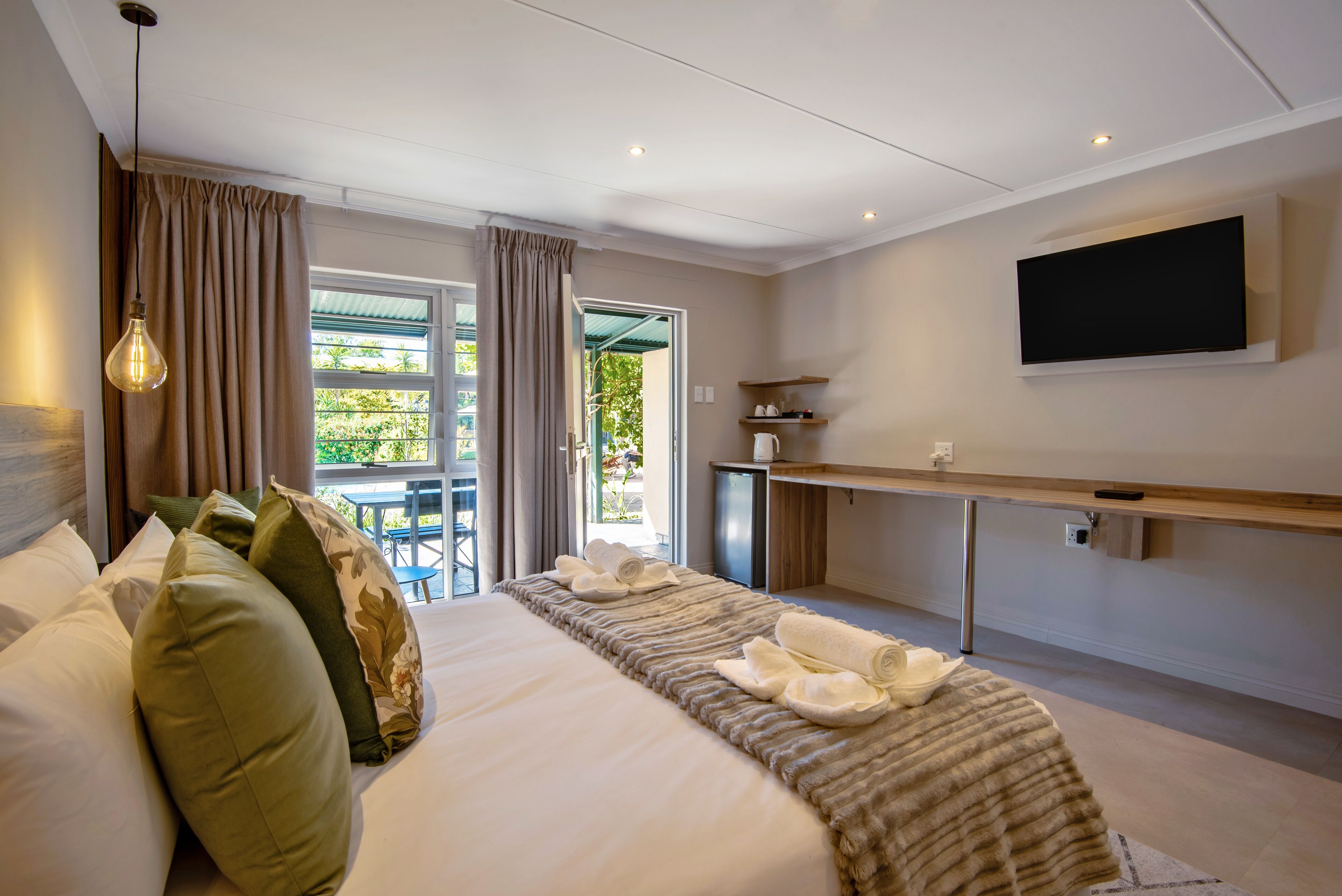 Quarto de hotel com cama, televisão, escrivaninha e vista para o exterior.
