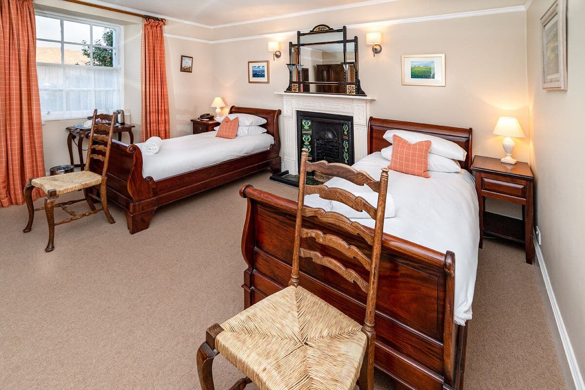 Quarto tradicional com duas camas de madeira, lareira, espelho e janela com cortinas.