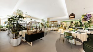 Um restaurante espaçoso com pé-direito alto, iluminação moderna e muitos vasos de plantas.