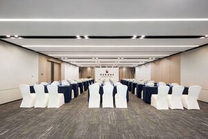 Uma sala de conferência com fileiras de mesas e cadeiras, um logotipo na parede e piso coberto de carpete.