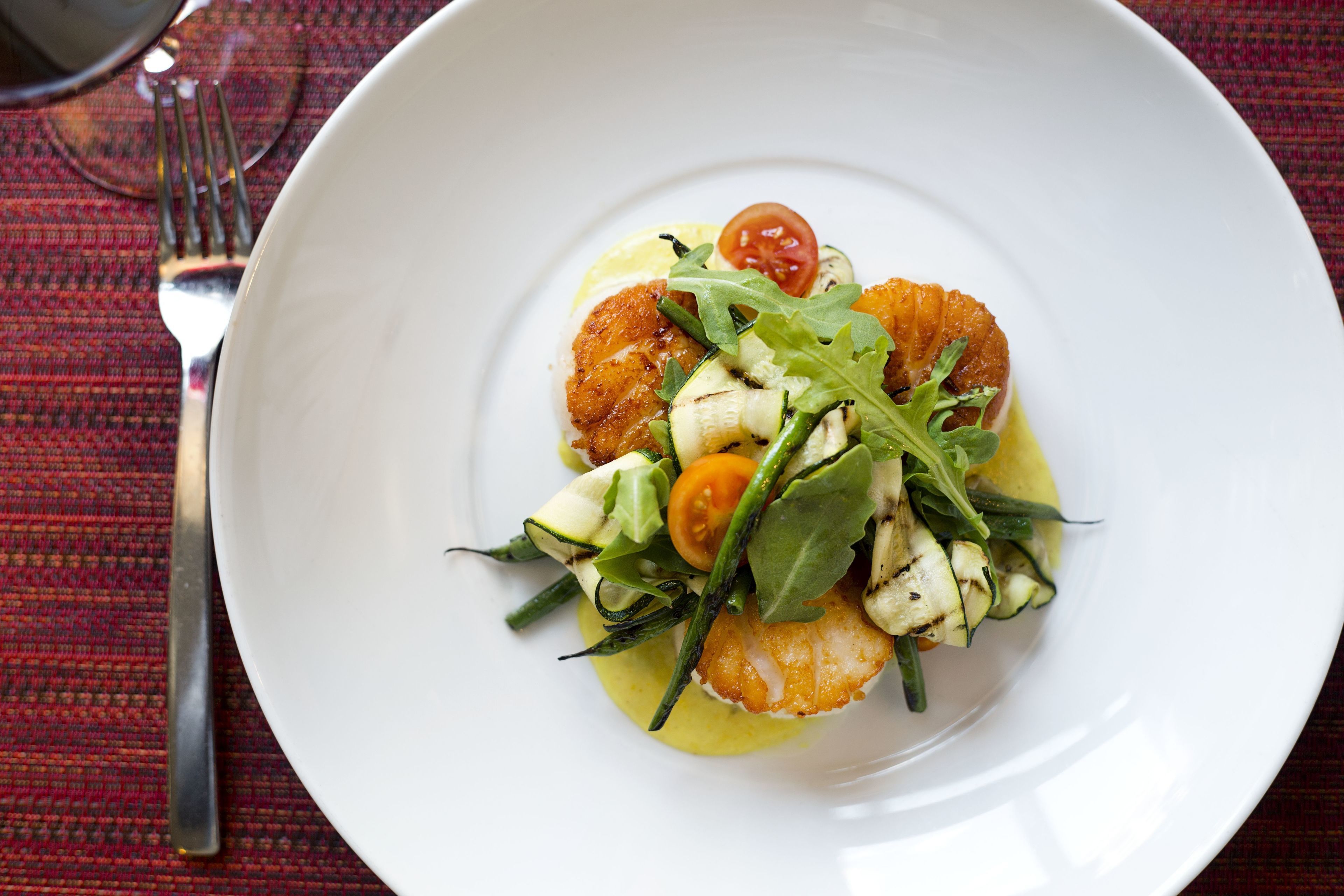 Um prato branco com um prato de frutos do mar, incluindo vieiras, aspargos, tomates cereja e um gajo de limão.