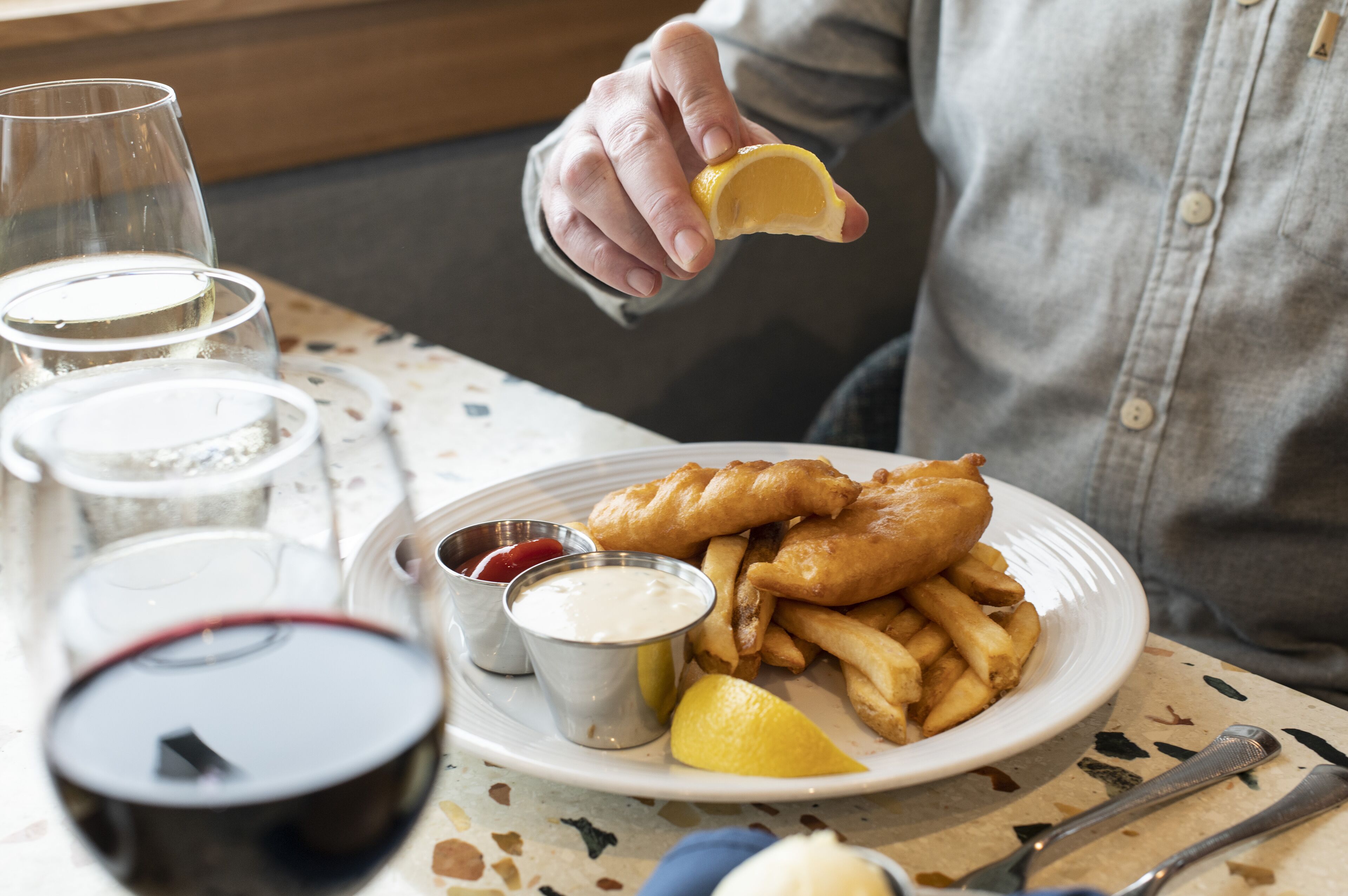 Prato de peixe com batatas fritas, acompanhado de gomos de limão e molhos sobre uma mesa.