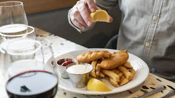 Prato de peixe com batatas fritas, acompanhado de gomos de limão e molhos sobre uma mesa.