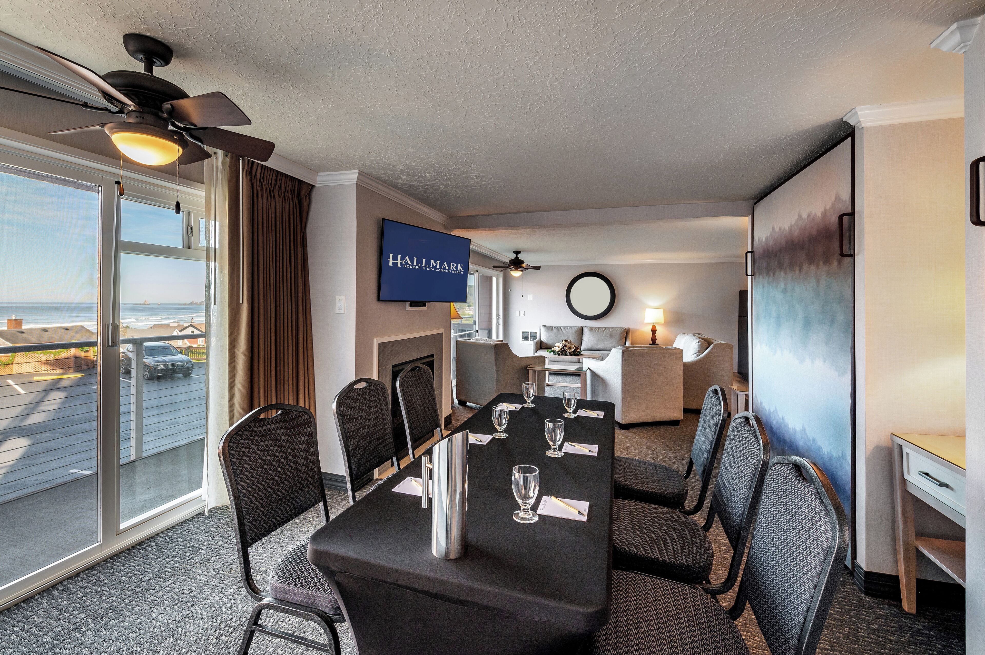 Quarto de hotel com uma mesa de conferências, cadeiras, televisão e vista para a praia.