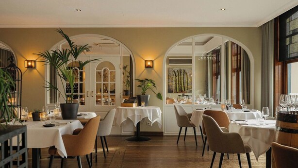 Restaurante com mesas postas, plantas em vasos e ambiente acolhedor.