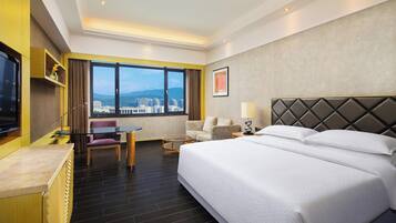 Quarto de hotel com uma cama grande, escrivaninha, cadeira e televisão.