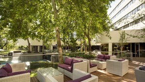 Uma área de lounge no terraço com móveis de vime, piscina e guarda-corpo de vidro.