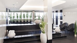 Uma área de spa moderna com hidromassagem, degraus de azulejos pretos e plantas em vasos.