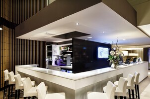 Uma área de bar moderna com máquina de café, assentos e uma placa com o horário de funcionamento.