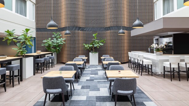 Restaurante moderno com área de estar central, bar à direita e parede de painéis de madeira verticais.