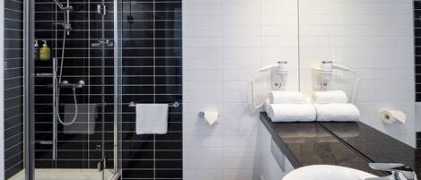 Casa de banho moderna com chuveiro em divisória de vidro, lavatório branco com bancada escura e sanita.