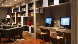 Quarto de hotel com escrivaninha, duas cadeiras, um sofá e uma estante.
