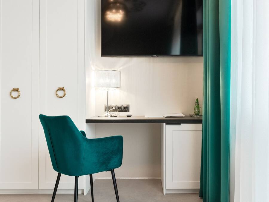 Quarto moderno com uma cadeira verde-água, uma escrivaninha com abajur e uma TV fixada na parede.