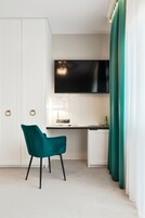 Quarto moderno com uma cadeira verde-água, uma escrivaninha com abajur e uma TV fixada na parede.