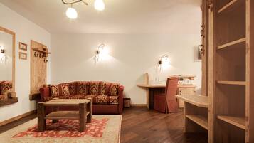 Uma sala de estar acolhedora com um sofá estampado, uma mesa de centro de madeira e um tapete vermelho. Há luminárias fixadas na parede e um armário de madeira.