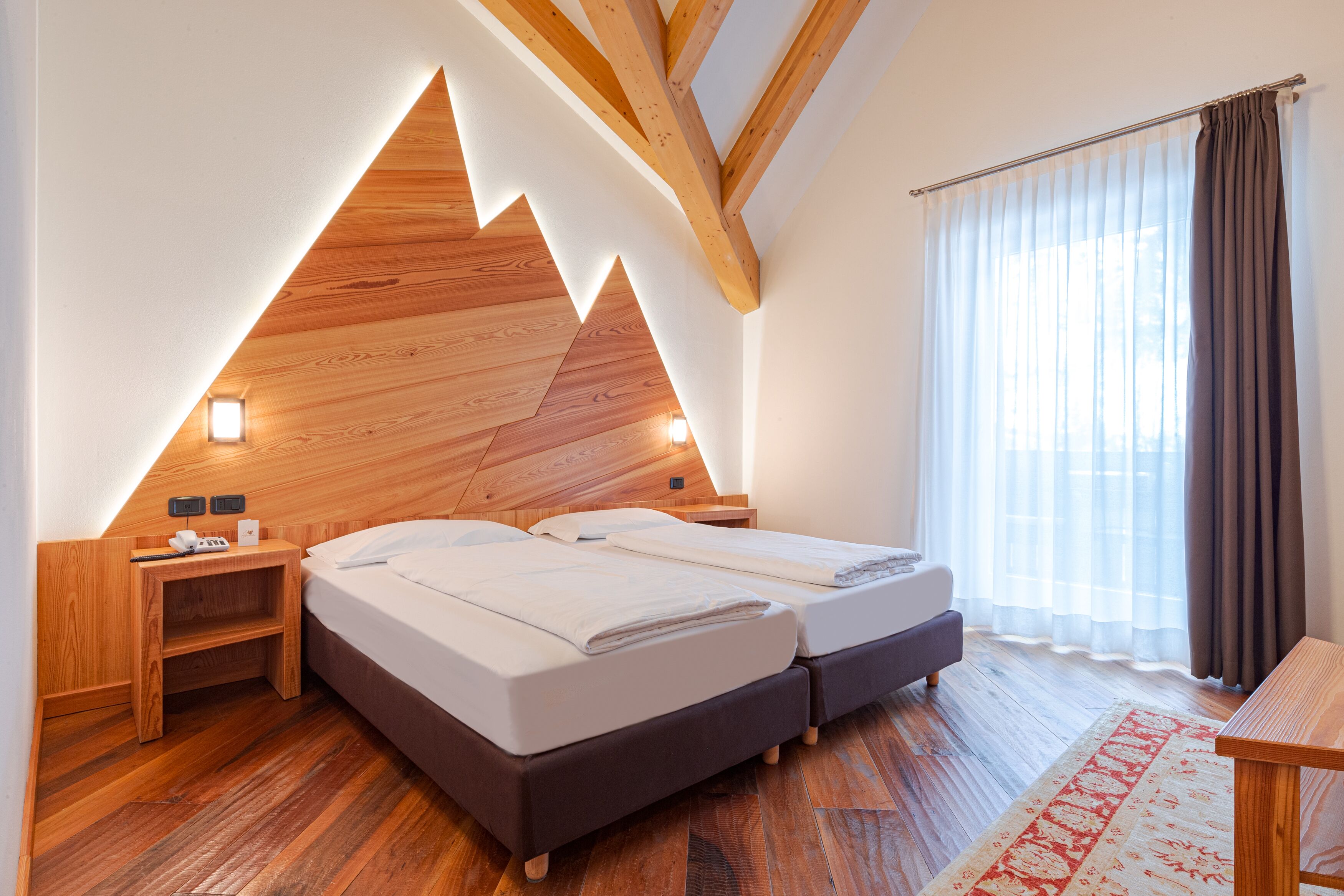 Quarto com teto de madeira, duas camas, uma mesinha de cabeceira e janela com cortinas.