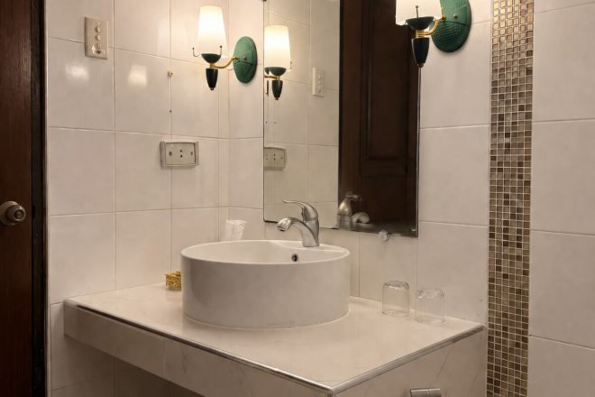 Uma casa de banho com uma pia branca, espelho e luzes na parede.