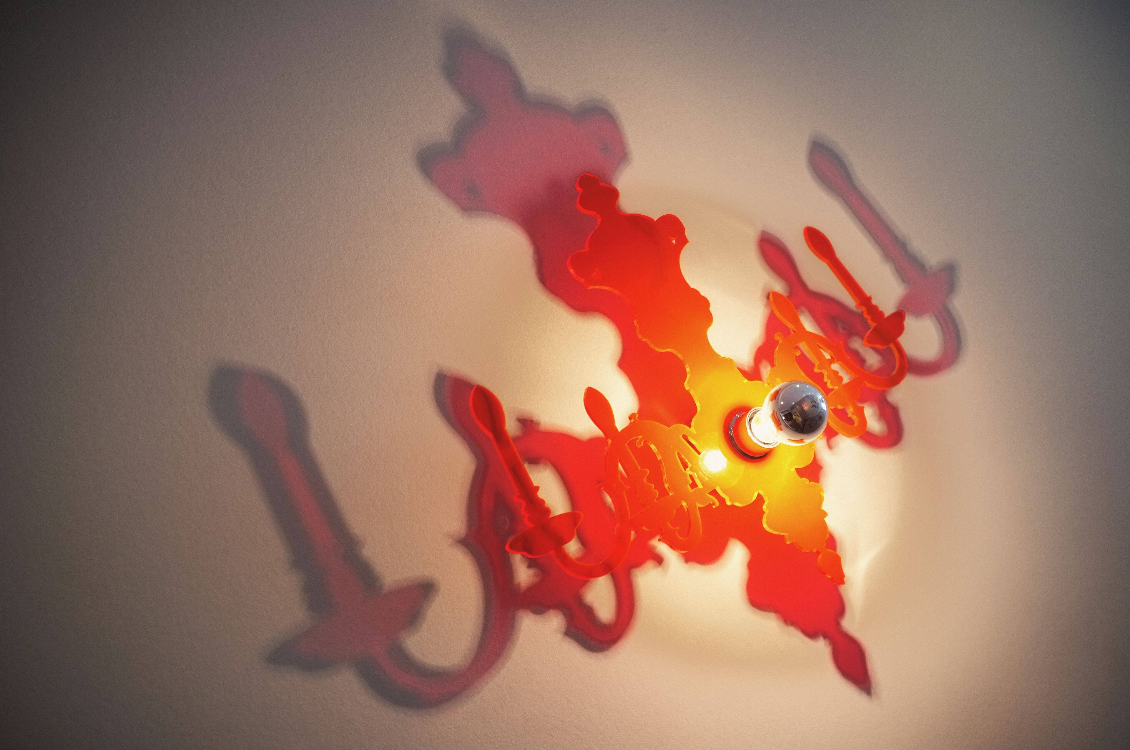 Luminária fixada na parede com design em vermelho e laranja.
