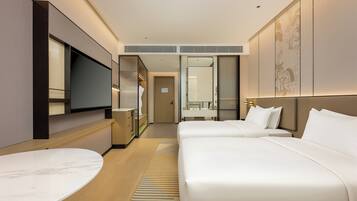 Quarto de hotel moderno com duas camas, televisão, escrivaninha e banheiro visível através de uma porta de correr.
