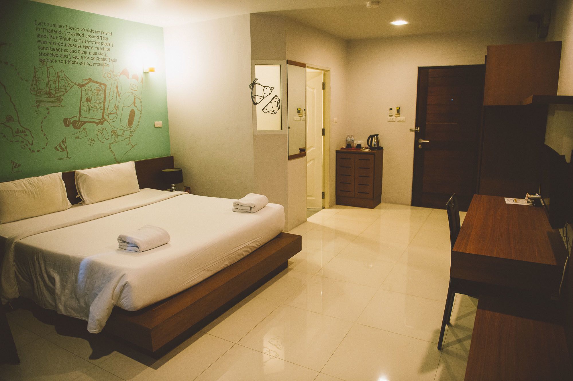 Quarto de hotel com uma cama grande, uma escrivaninha, um guarda-roupa e uma parede verde com um mapa.