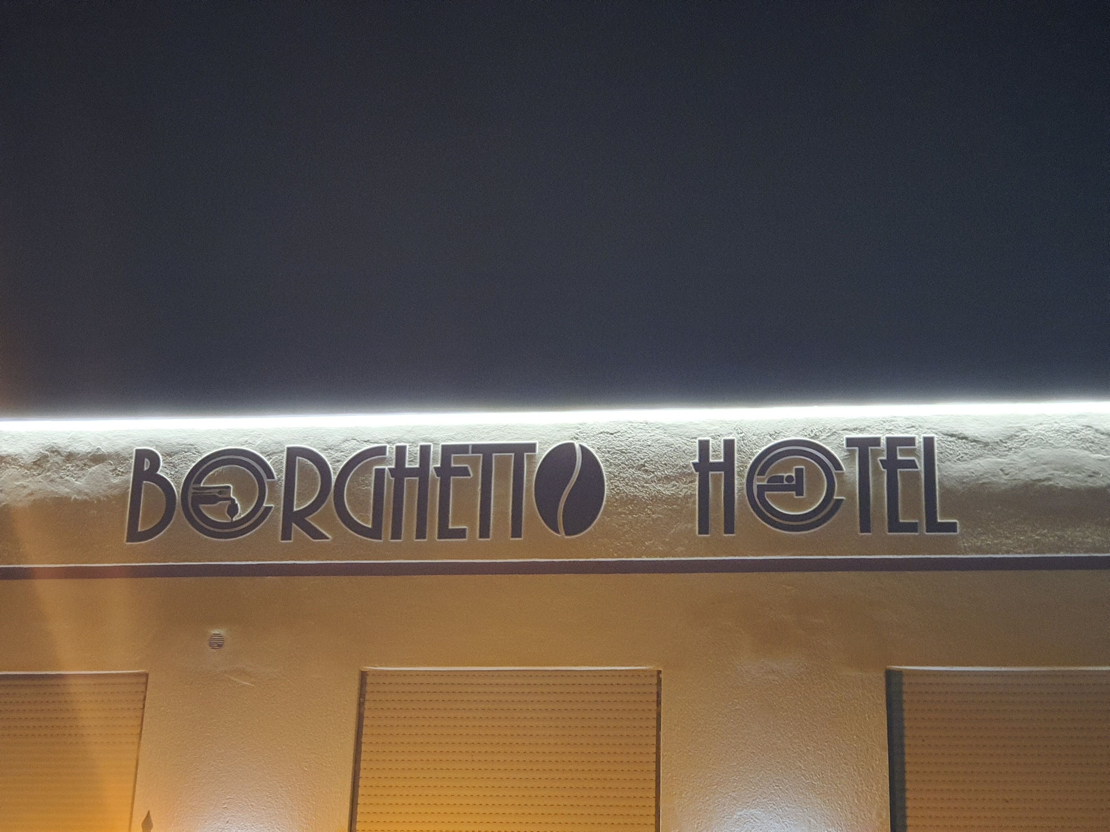 Placa de hotel com o nome 'BORGHETO HOTEL' iluminado.