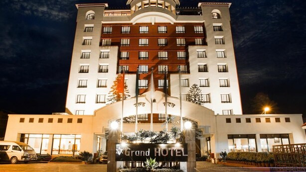 Um Grand Hotel com entrada central, vários andares e fachada bem iluminada.