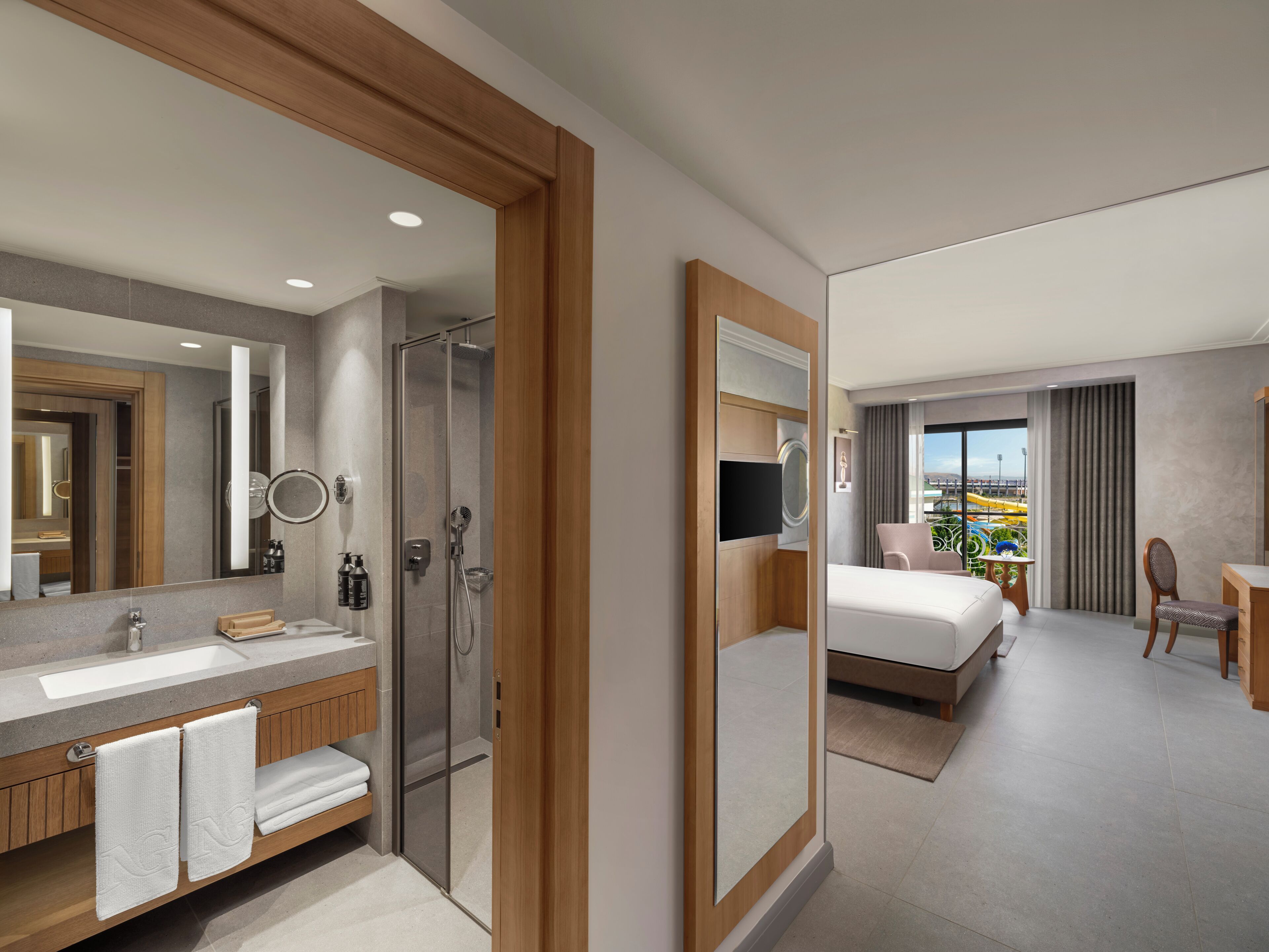 Quarto de hotel moderno com chuveiro, uma cama grande, uma mesa de escritório e vista para um jardim.