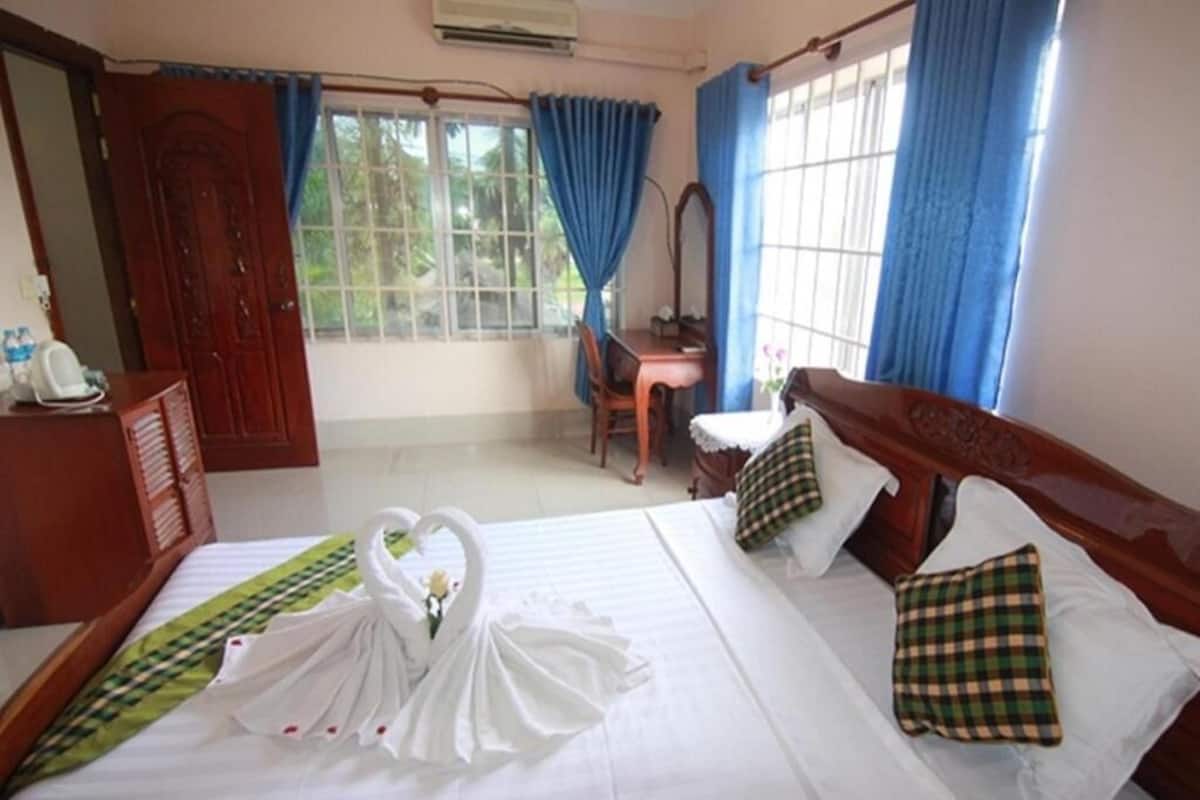 Quarto de hotel com cama, escrivaninha, cadeira e janela com cortinas.
