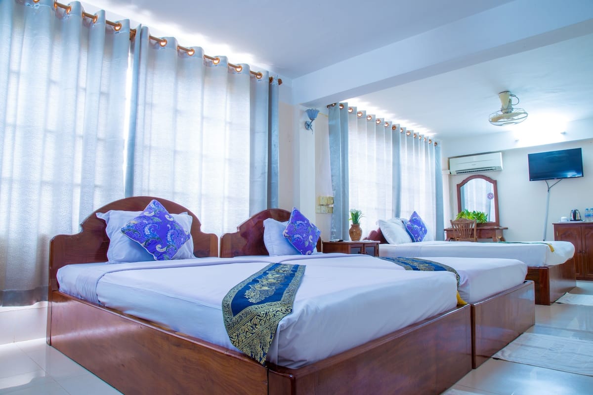 Quarto de hotel com duas camas de madeira, uma televisão e um ventilador de teto.