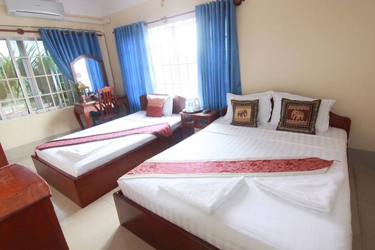 Quarto de hotel com duas camas, uma mesa, uma cadeira e janela com cortinas.