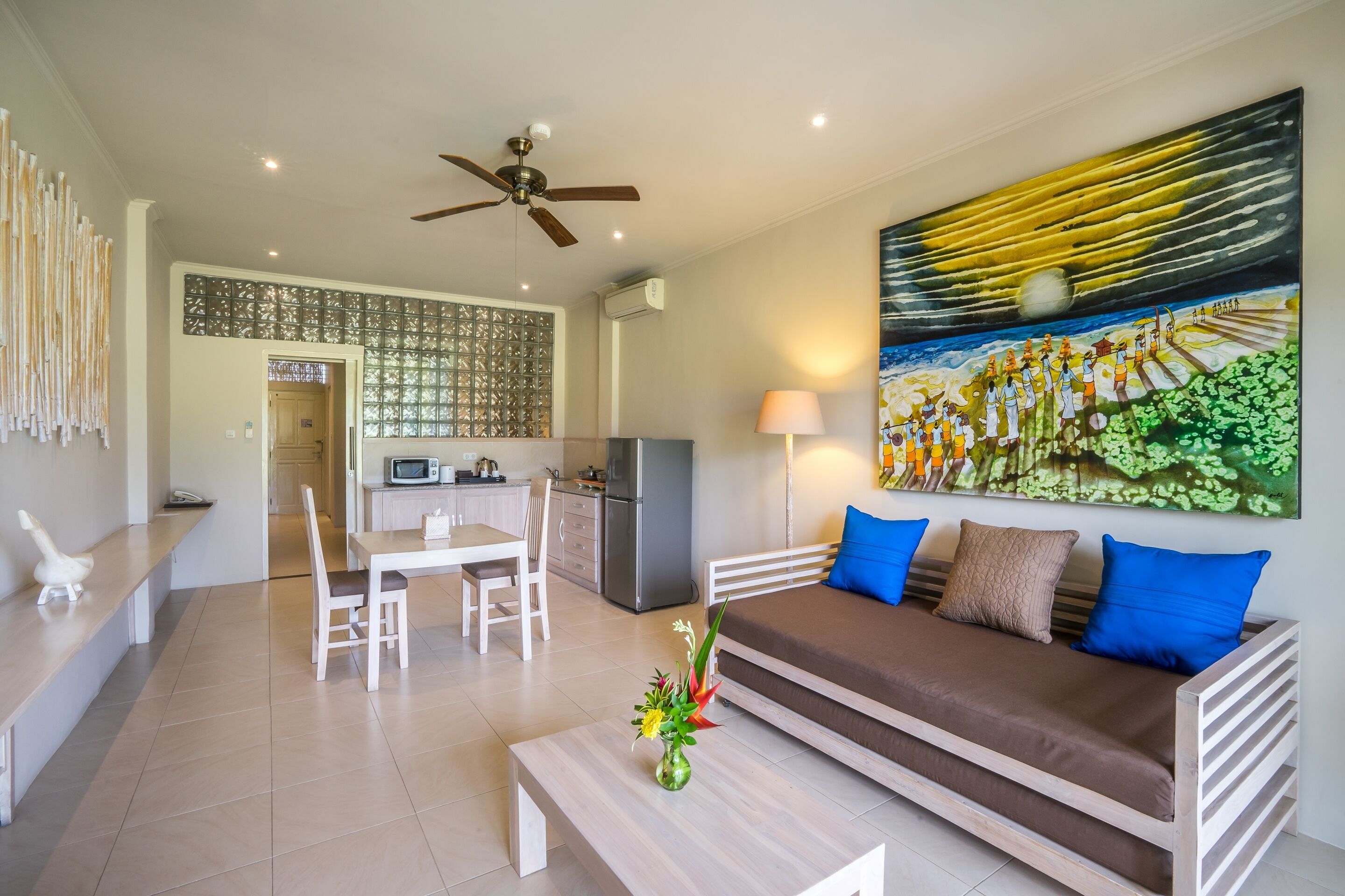 Uma sala de estar moderna com sofá, mesa de centro e área de jantar. Há um quadro na parede e um ventilador de teto.