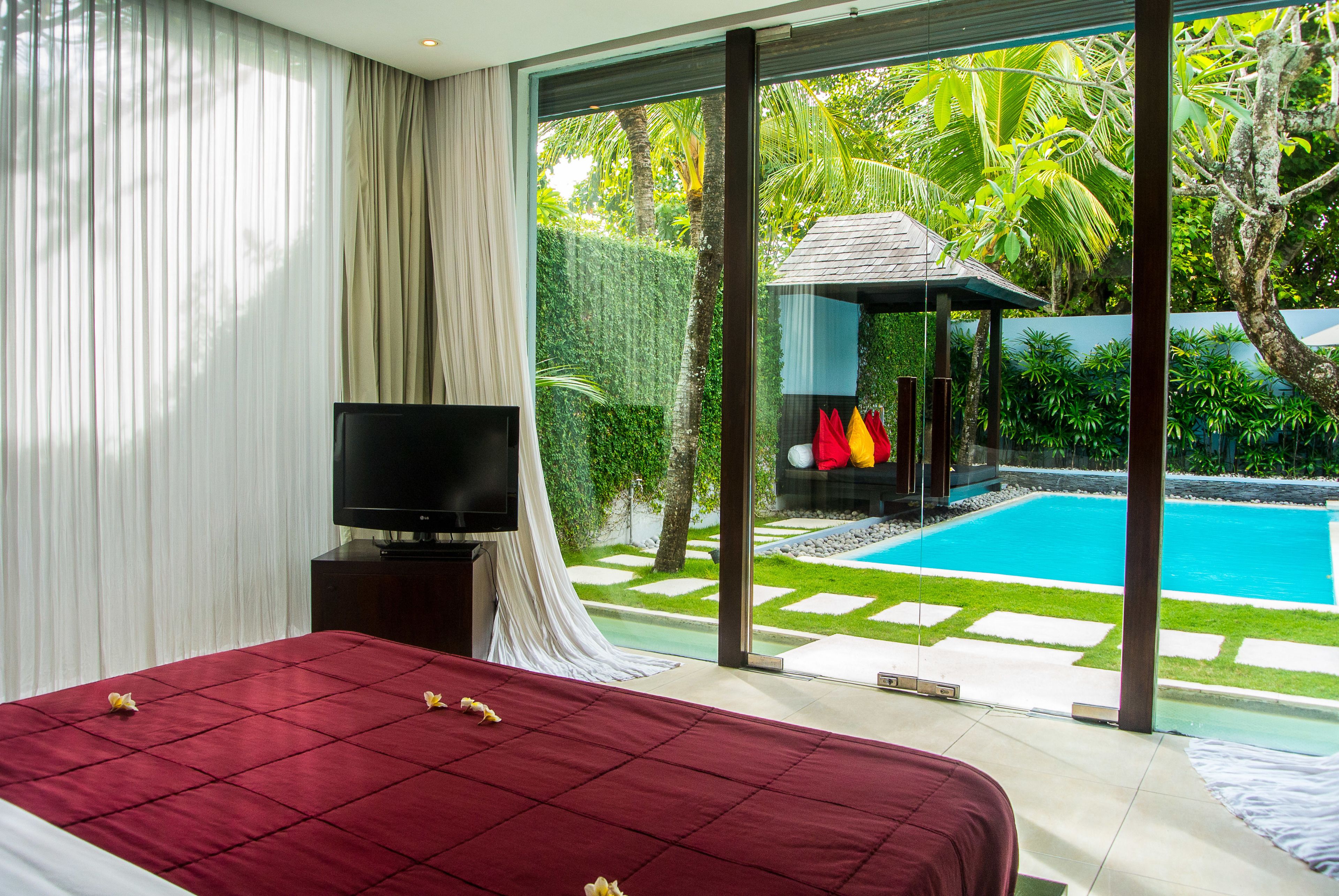 Quarto com cama grande, televisão e vista para piscina e área externa.