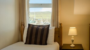 Uma cama com um travesseiro listrado e um travesseiro branco, uma mesa de cabeceira com uma luminária, e vista para um porto através de uma janela.