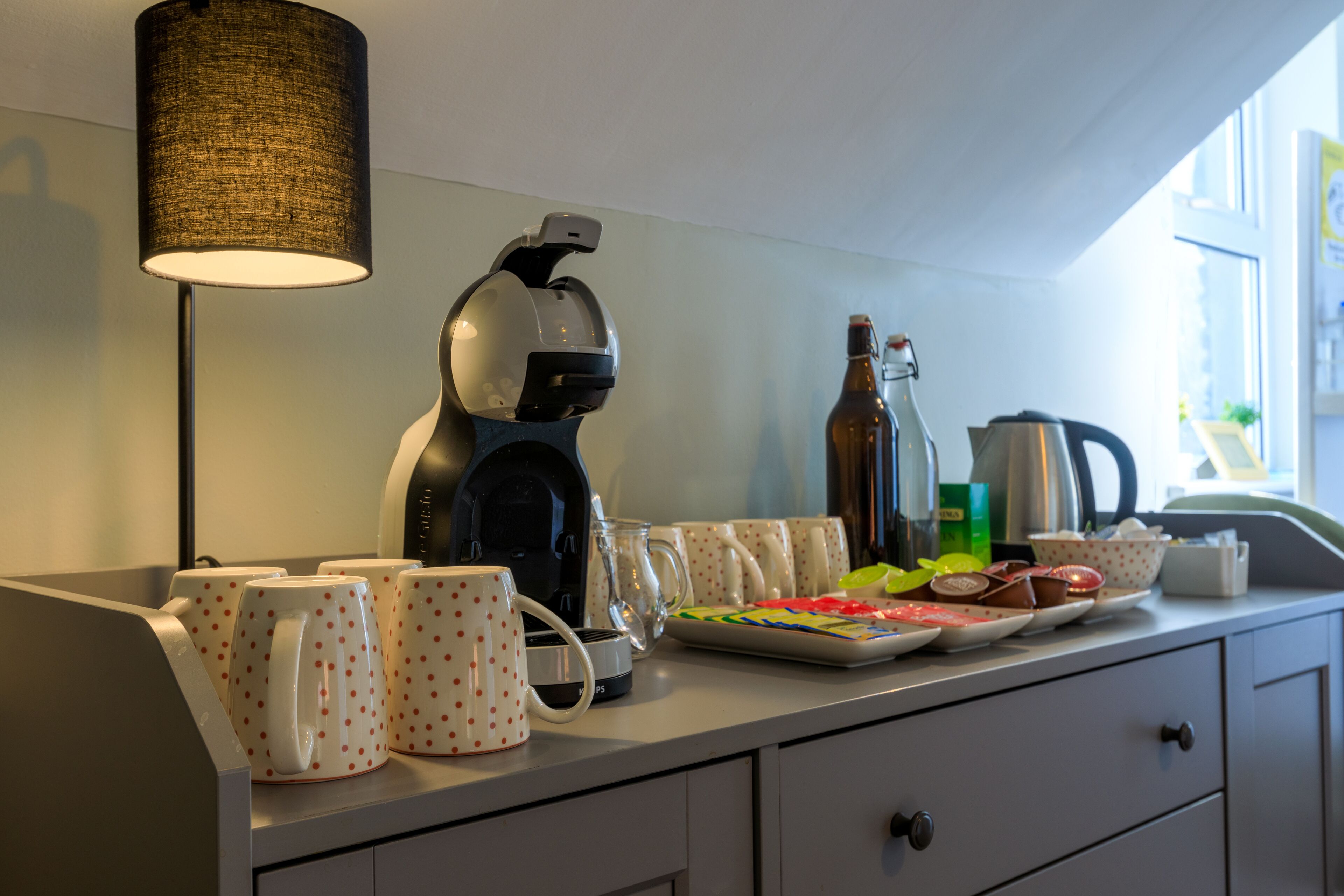 Uma bancada de cozinha com uma cafeteira, chávenas, um prato de comida e uma chaleira.