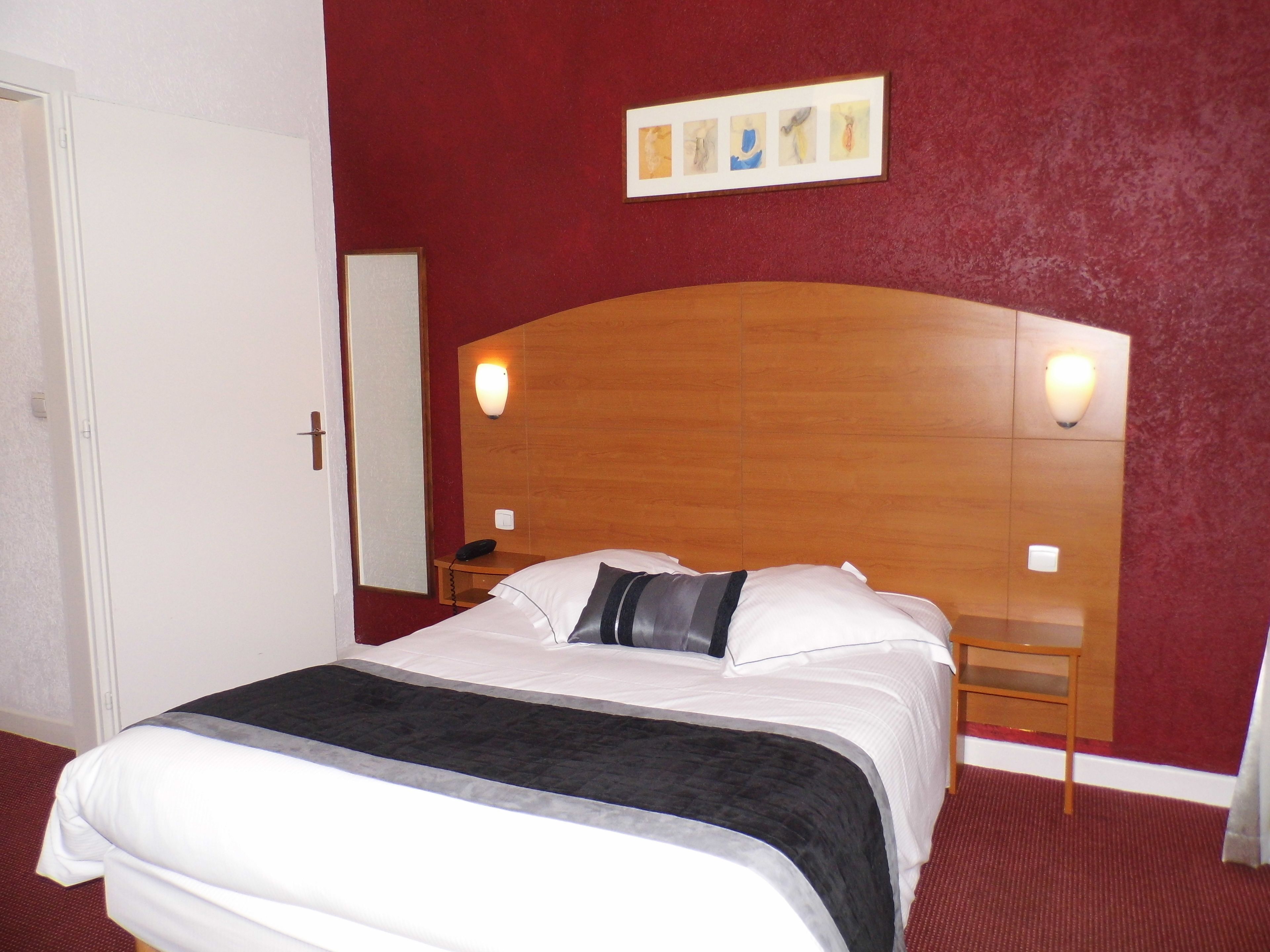 Quarto de hotel com uma cama grande, cabeceira de madeira, mesas de cabeceira e uma obra de arte pendurada na parede.