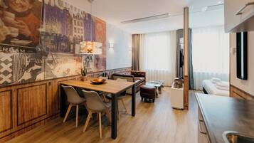 Quarto de hotel moderno com mesa de jantar de madeira, cadeiras, sofá, mesa de centro pequena e uma cama.