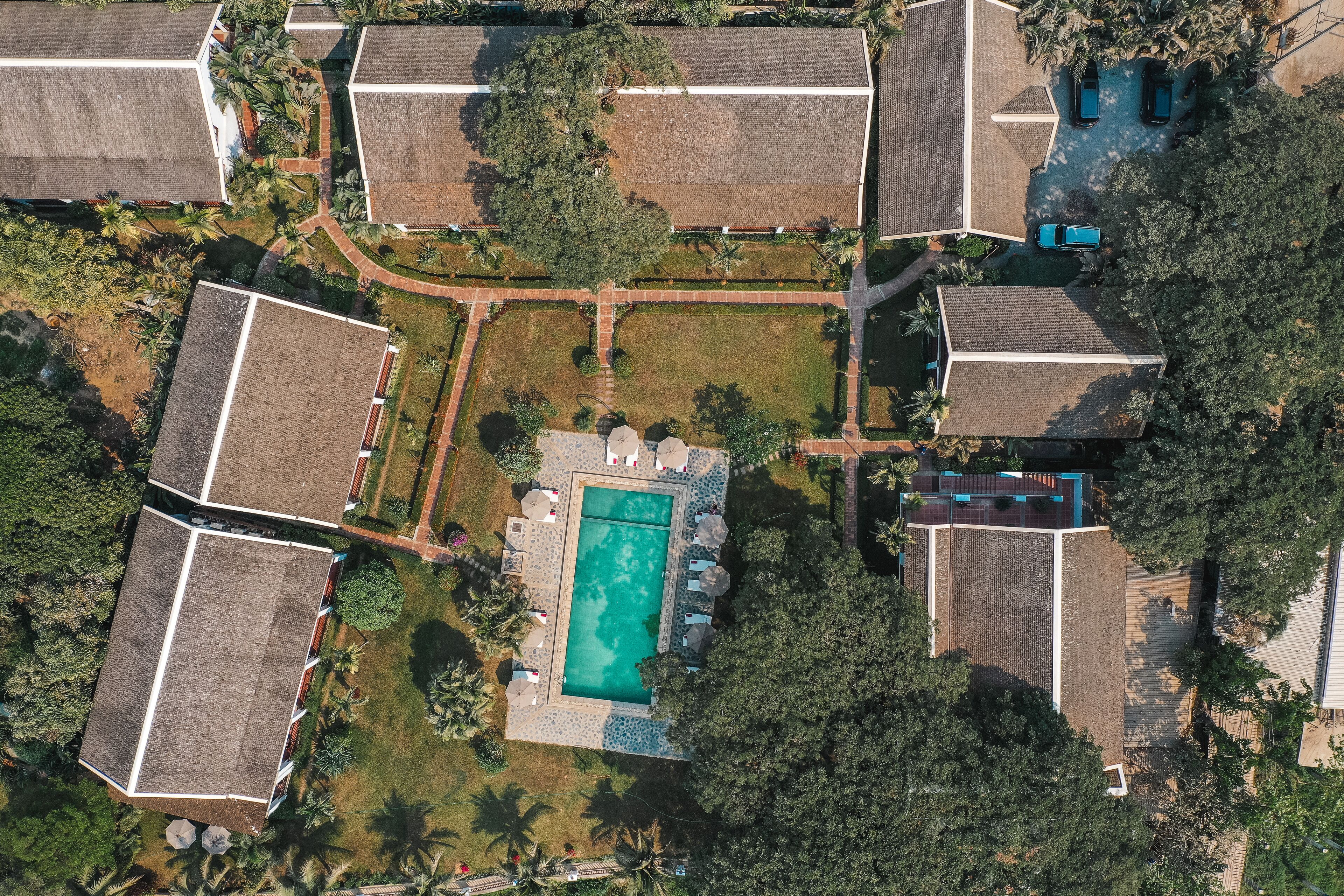 Vista aérea de uma área residencial com várias casas, uma piscina central e vegetação ao redor.